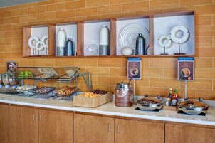Buffet de café da manhã com diversas opções de alimentos, incluindo frutas, doces e uma máquina de café.