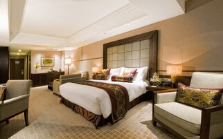 Quarto de hotel com uma cama grande, duas mesas de cabeceira, uma cadeira, uma escrivaninha e um abajur.