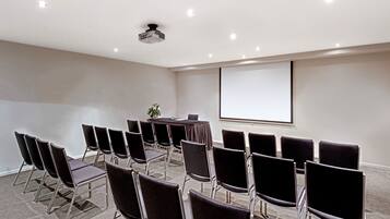 Uma sala de conferências com projetor, tela e fileiras de cadeiras.