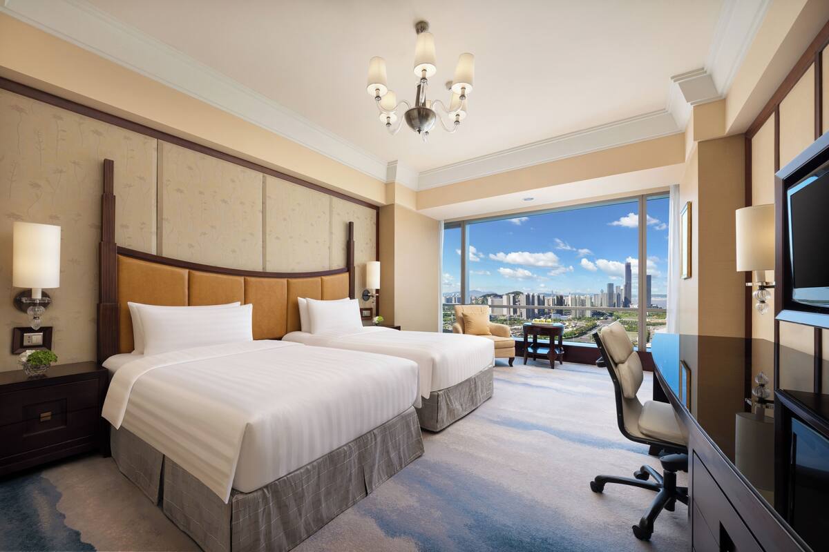 Quarto de hotel com duas camas, uma escrivaninha, uma cadeira e uma televisão.