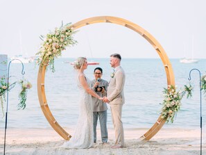 Cerimônia de casamento com um arco de madeira e decorações florais na praia.