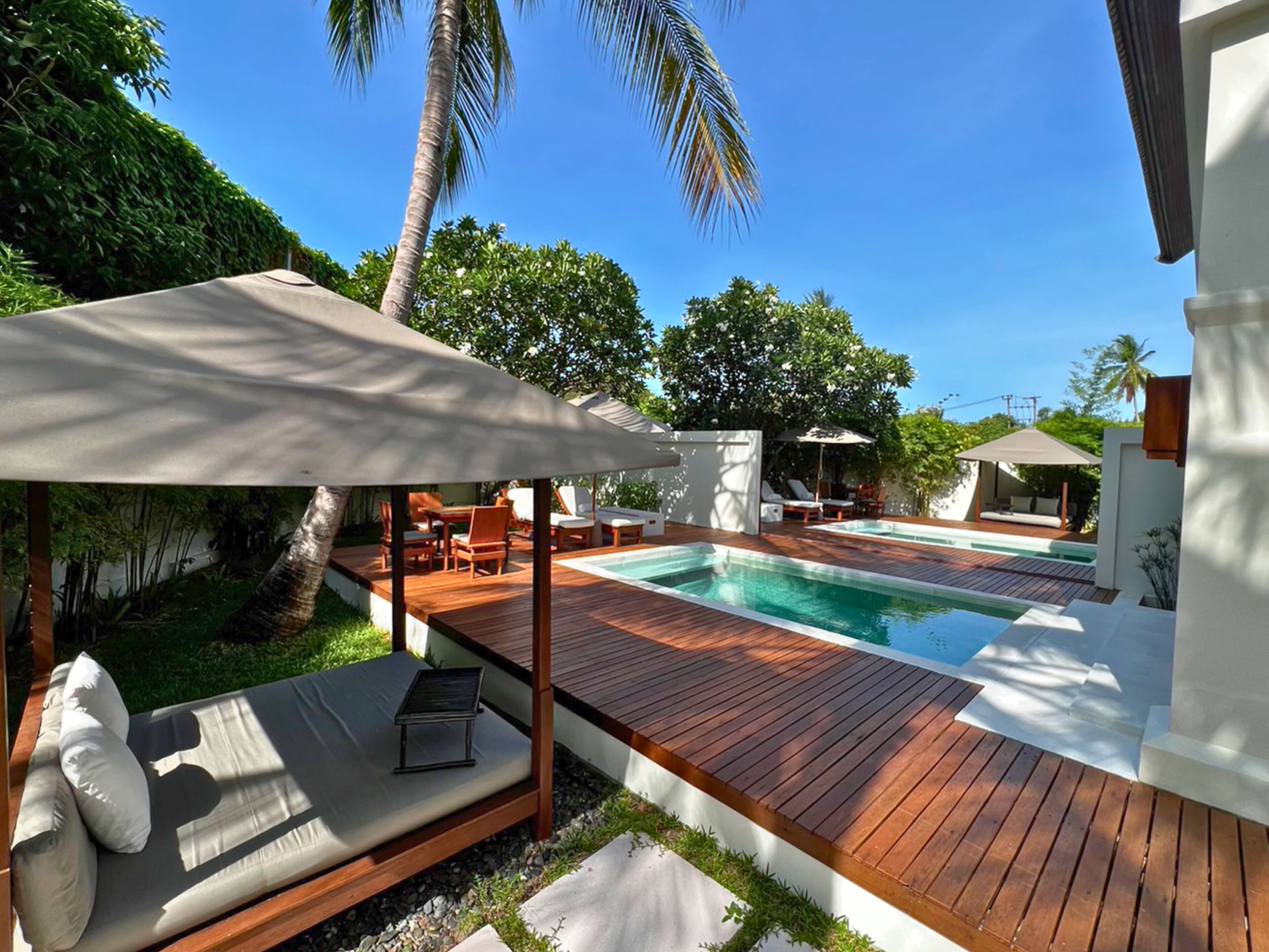 Área de piscina com deck de madeira, espreguiçadeiras e guarda-sóis.