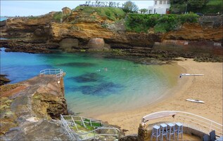 Uma praia costeira com águas claras, areal arenoso e um penhasco rochoso.