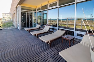 Um terraço com espreguiçadeiras de madeira e uma parede de vidro com vista para a paisagem.