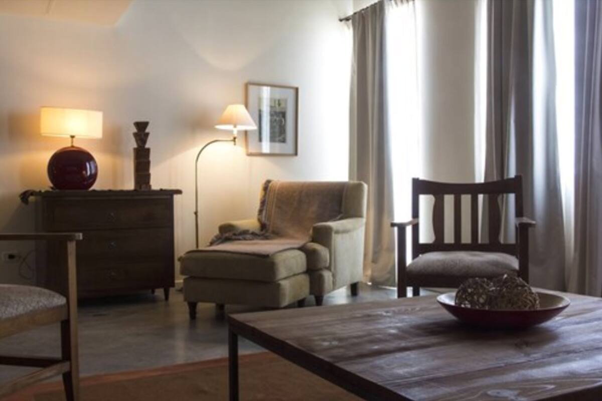 Uma sala de estar com sofá, poltrona, mesa de centro de madeira e um abajur.