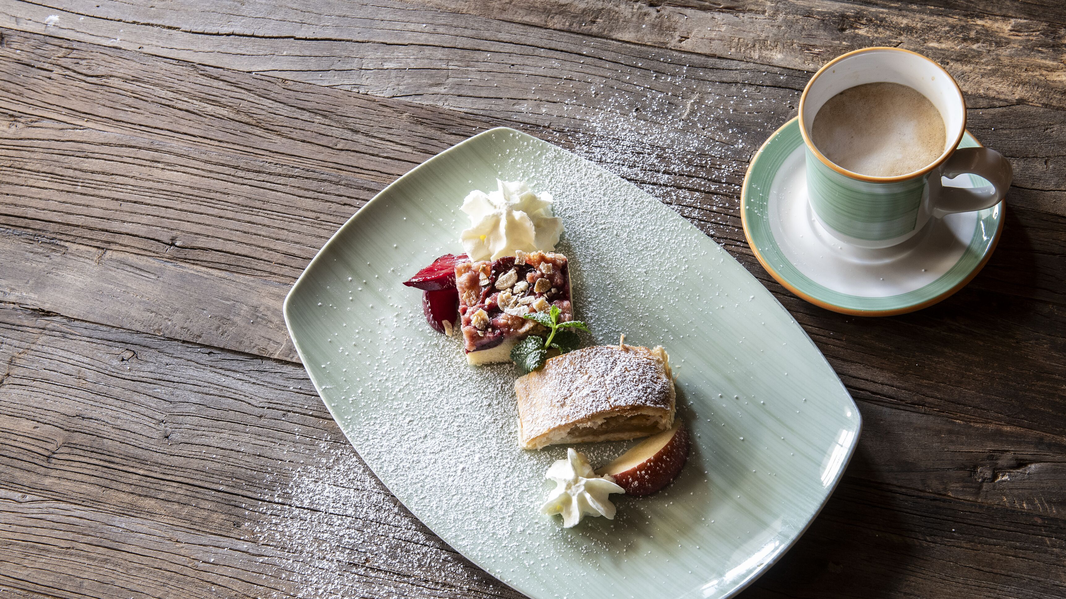 Um prato de sobremesa com um pastel, chantilly e frutas vermelhas sobre uma mesa de madeira.
