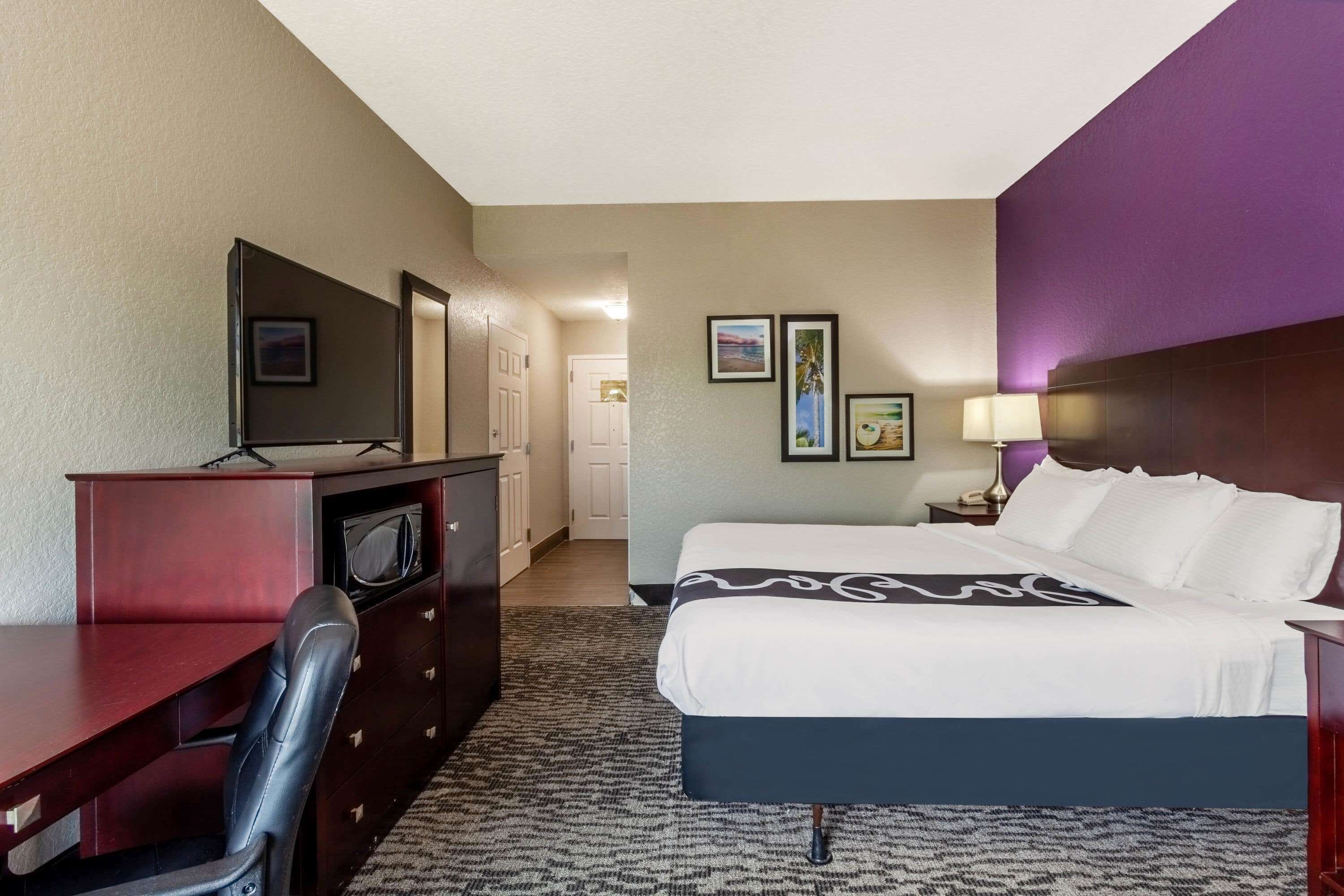 Quarto de hotel com cama, escrivaninha, cadeira e televisão.