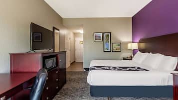 Quarto de hotel com cama, escrivaninha, cadeira e televisão.