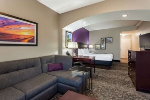 Quarto de hotel com sofá, cama, escrivaninha e televisão.