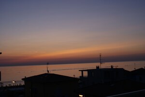 Vista de um pôr do sol na costa, com edifícios ao primeiro plano.