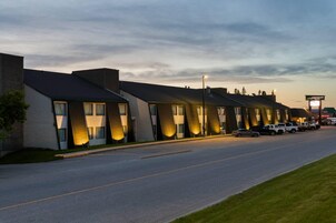 Fileira de edifícios de motel modernos com janelas iluminadas, céu claro e uma estrada com veículos estacionados.