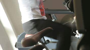 Uma pessoa usando uma bicicleta ergométrica em um espaço com esteira e aparelhos de ginástica.