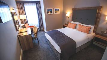 Quarto de hotel com uma cama grande, uma escrivaninha, uma cadeira e uma mesa de cabeceira.