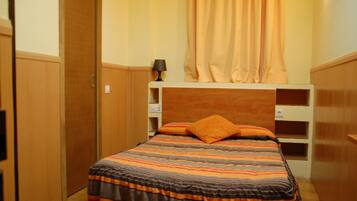 Quarto com cama, mesa de cabeceira, abajur e janela com cortinas.