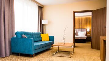 Quarto de hotel com sofá azul, uma pequena mesa de madeira, luminária e cama com cabeceira de madeira.