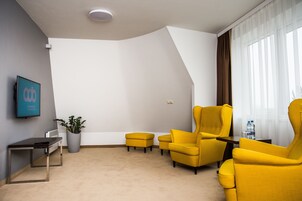 Quarto de hotel moderno com um sofá, uma mesinha, um vaso de planta e uma TV de tela plana na parede.