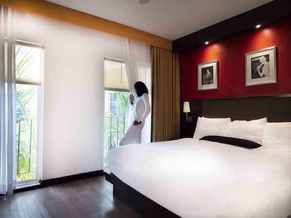 Quarto de hotel com uma cama grande, janela com cortinas, cabeceira e duas imagens emolduradas na parede.