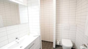 Um banheiro moderno com azulejos brancos, pia branca com torneira cromada, vaso sanitário e área de chuveiro.