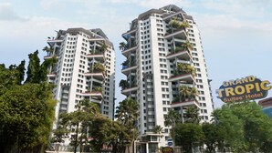 Dois edifícios altos com varandas, um letreiro do Hotel 'Grand Tropic Suites' e vegetação ao redor.