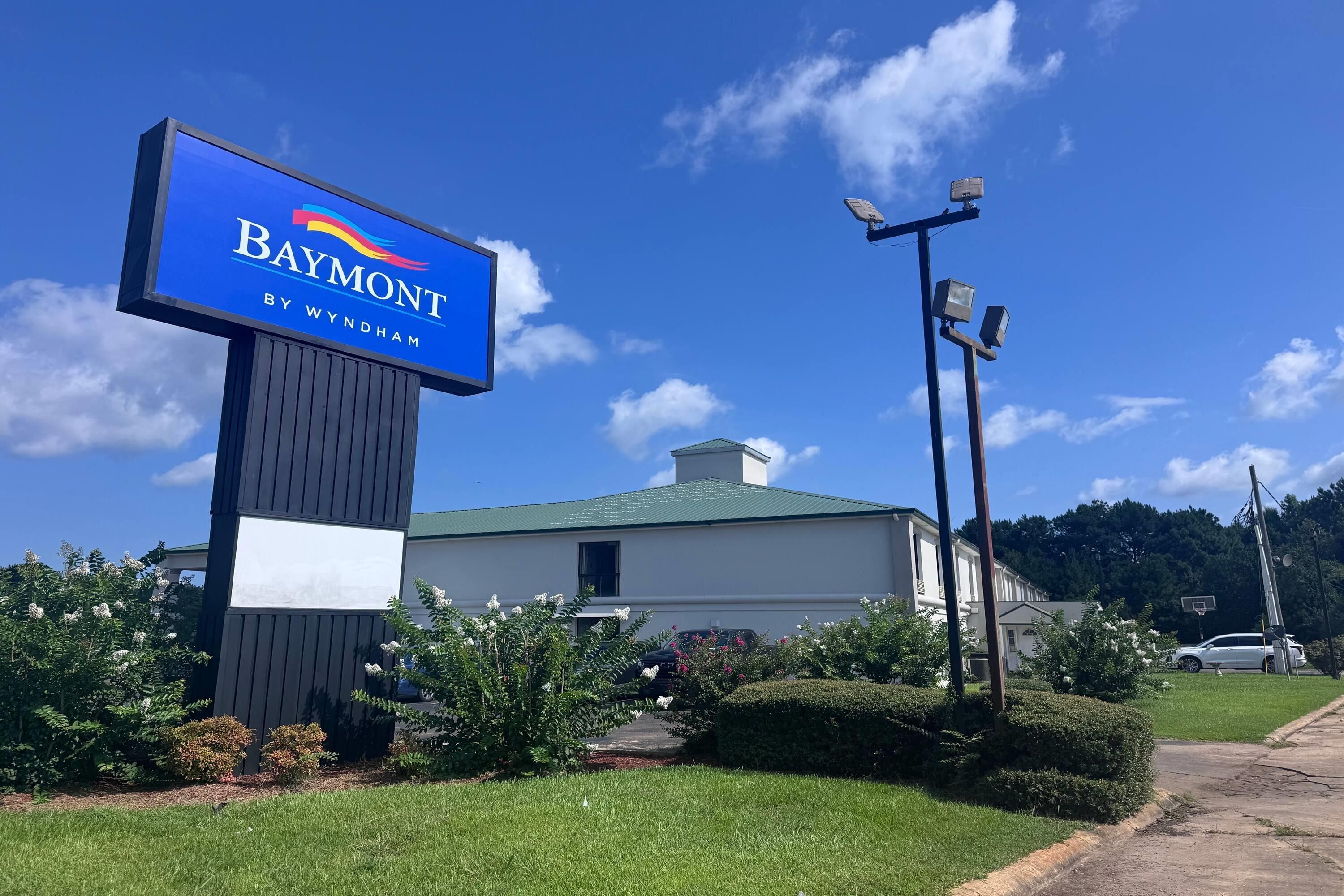 Placa da Baymont by Wyndham, um edifício com telhado verde e área de estacionamento com um carro branco.