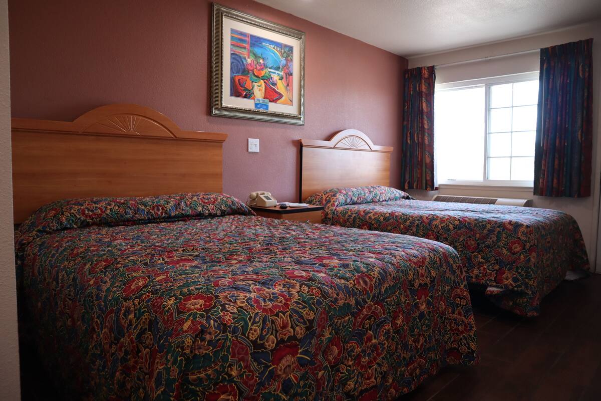 Quarto de hotel com duas camas, cabeceira de madeira, um quadro na parede e uma janela com cortinas.