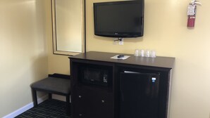 Quarto de hotel com televisão de tela plana na parede, minibar, um banco e extintor de incêndio.