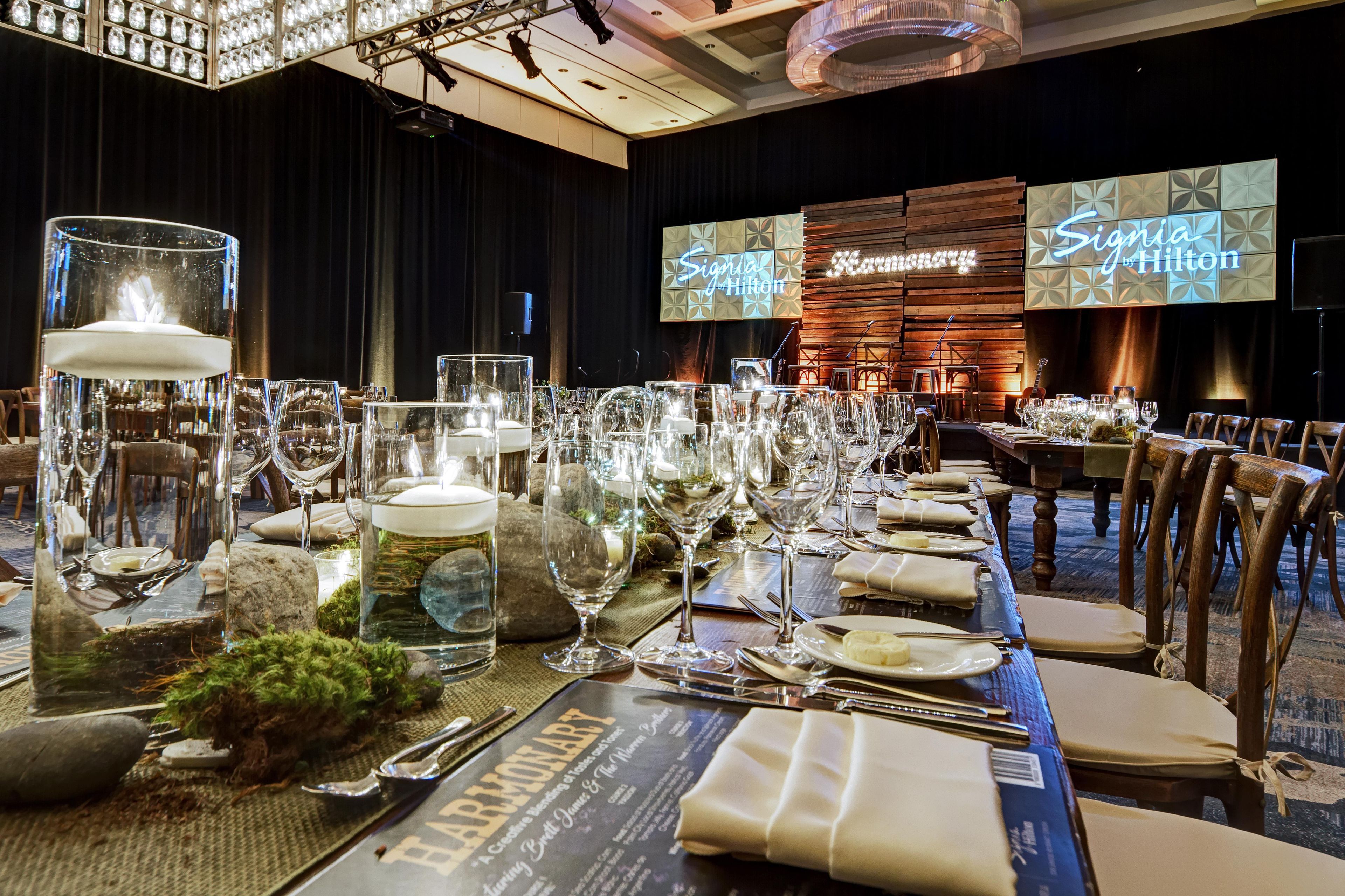 Salão de banquetes com longas mesas dispostas para um evento formal, incluindo taças, pratos e talheres.