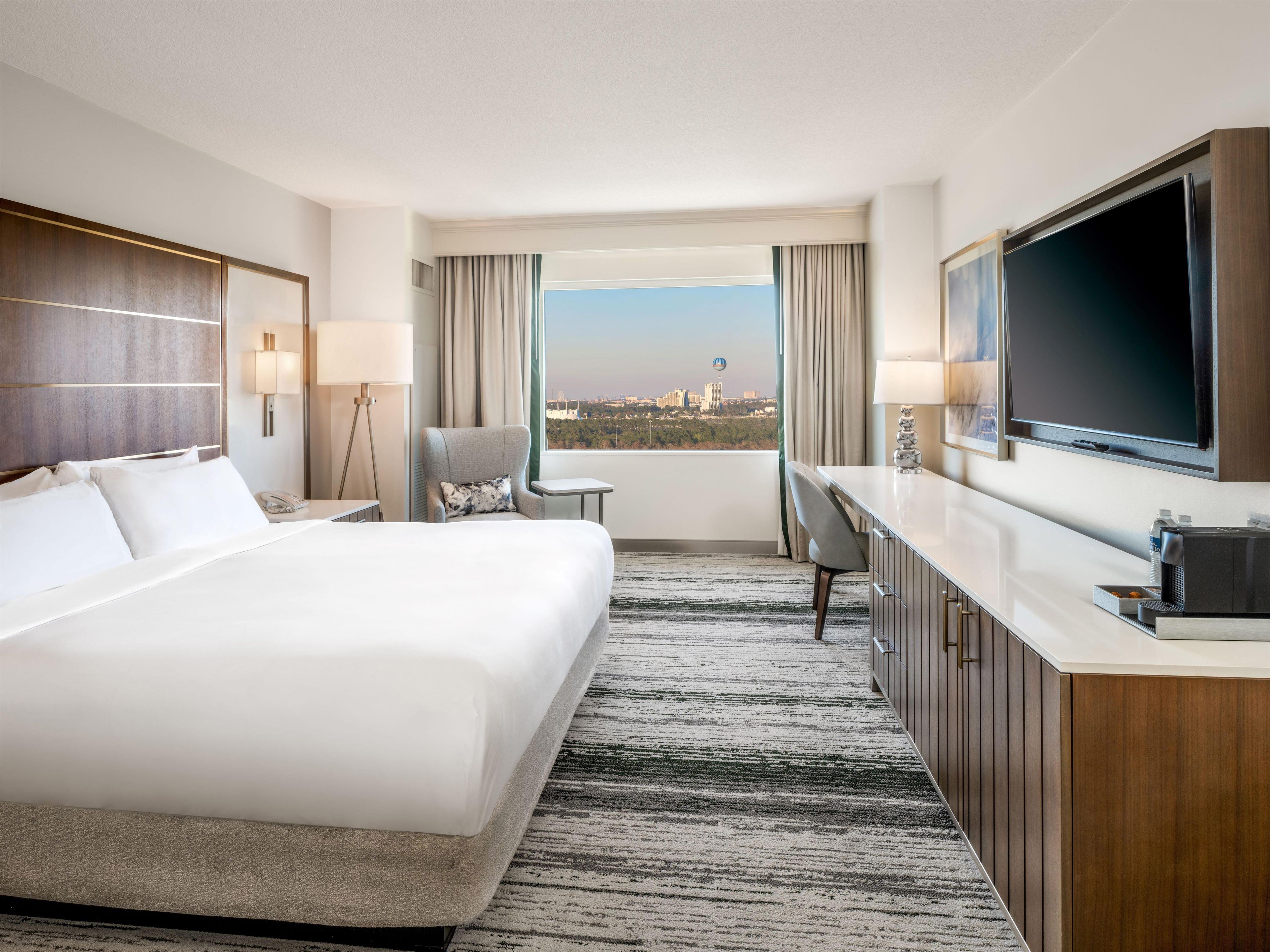 Quarto de hotel com cama, escrivaninha, cadeira, televisão e vista para a cidade.