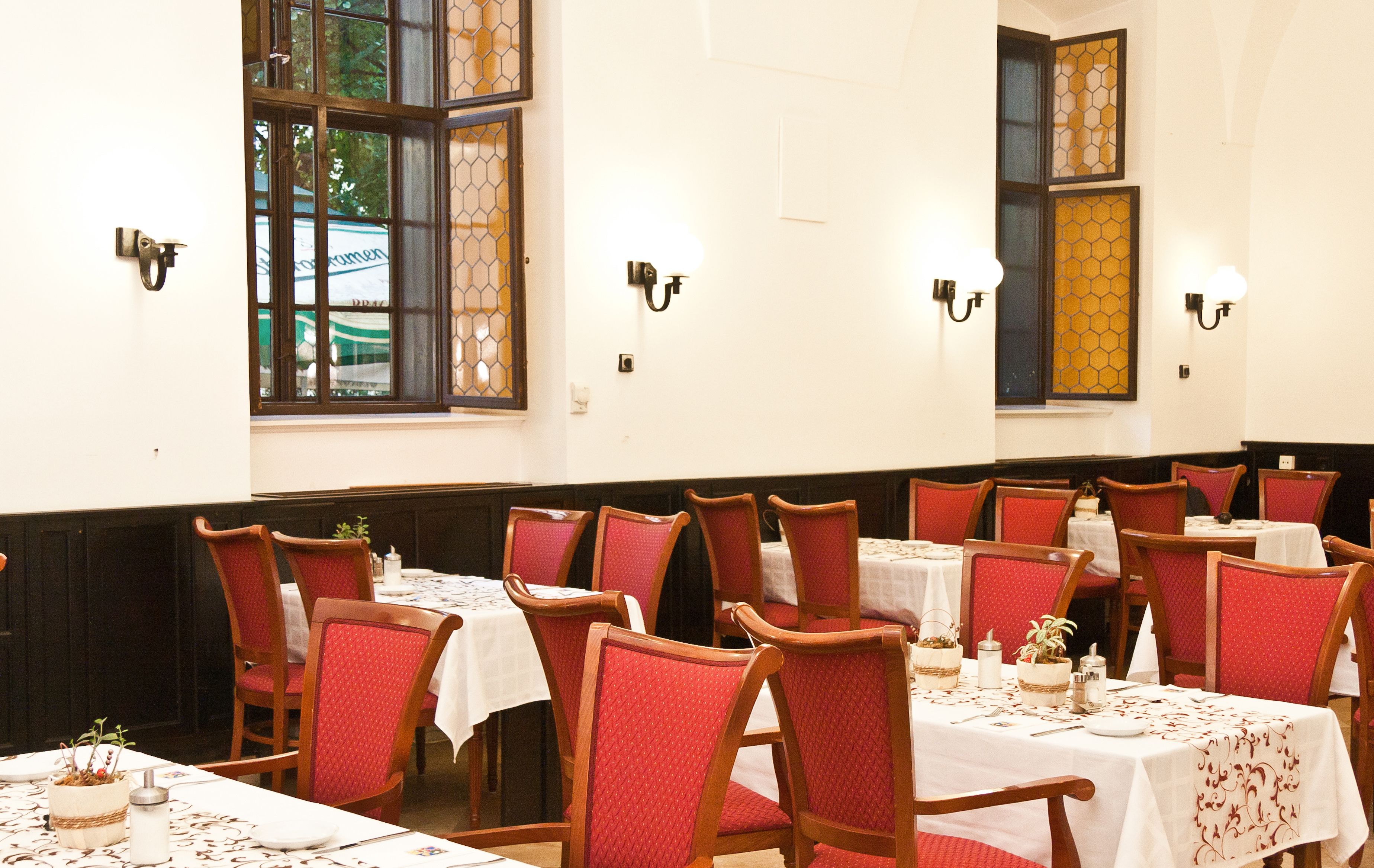 Um restaurante com várias mesas e cadeiras, cada conjunto com toalhas brancas e cadeiras vermelhas.