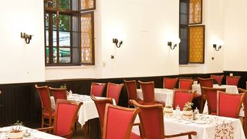 Um restaurante com várias mesas e cadeiras, cada conjunto com toalhas brancas e cadeiras vermelhas.