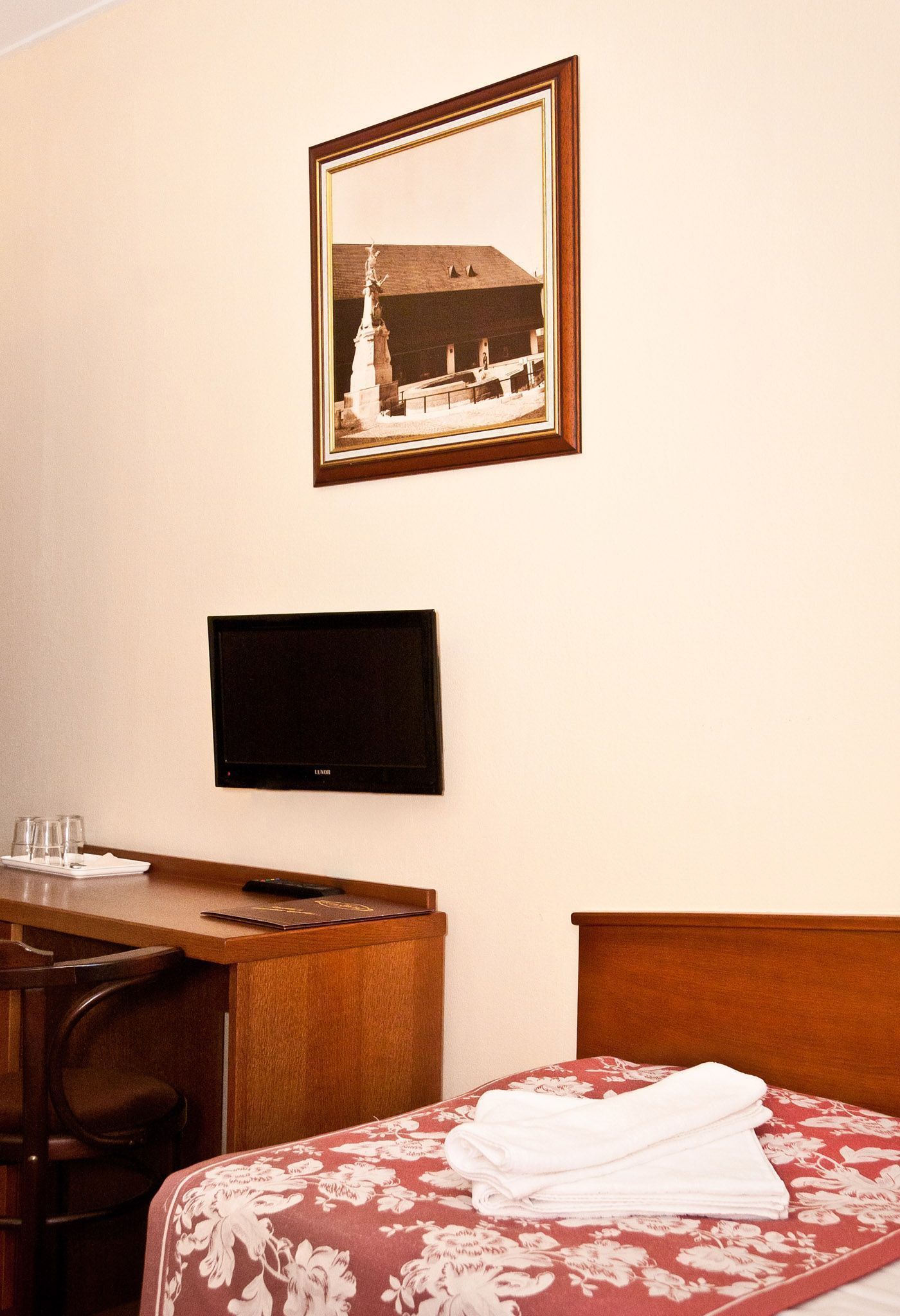 Quarto de hotel com cama, escrivaninha, cadeira, televisão e quadro na parede.