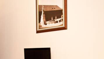 Quarto de hotel com cama, escrivaninha, cadeira, televisão e quadro na parede.