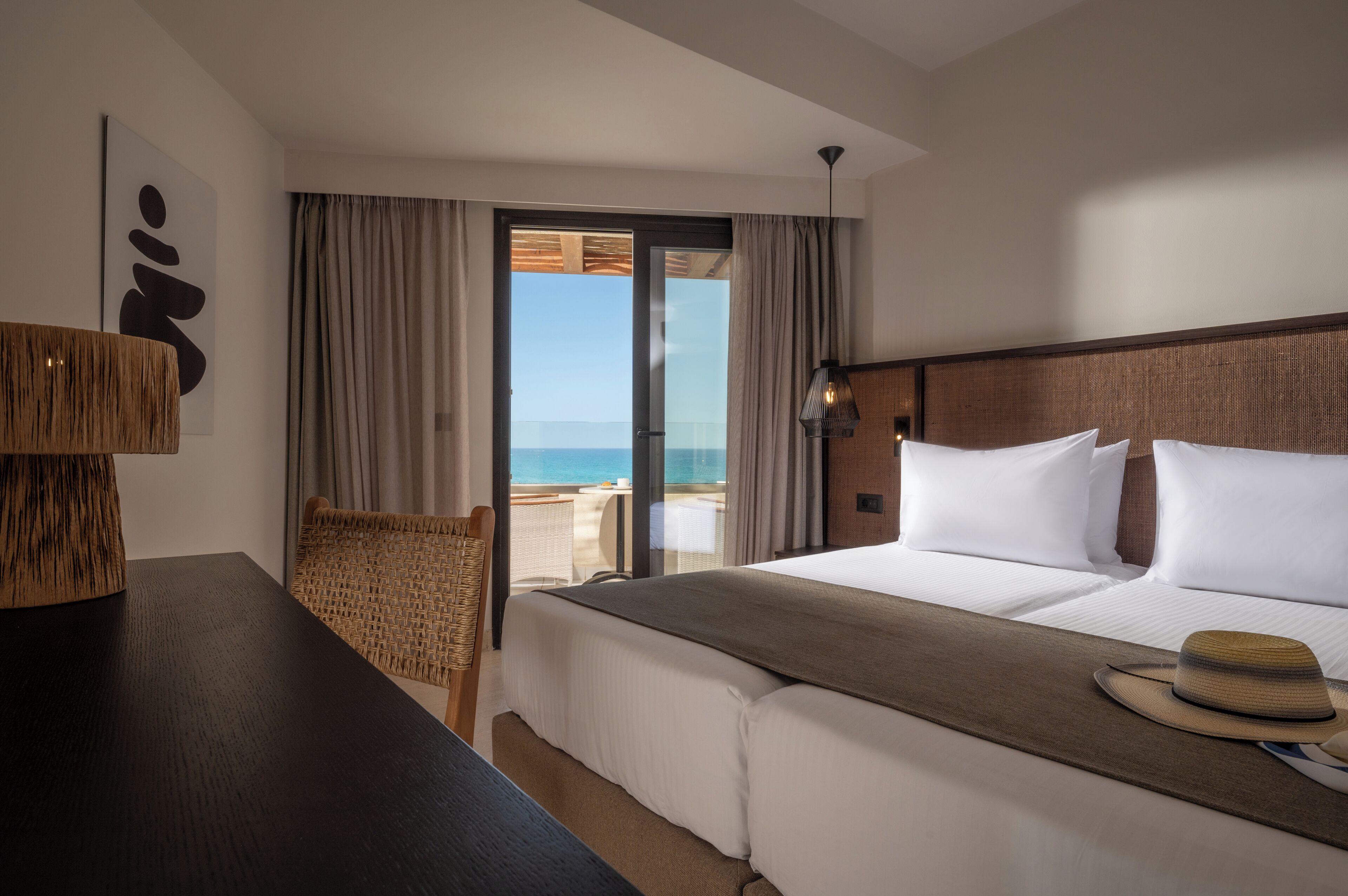 Quarto de hotel com uma cama, uma cadeira, uma mesa, um abajur e vista para o mar.