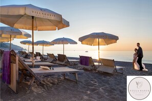 Praia particular, areia preta, espreguiçadeiras, guarda-sóis