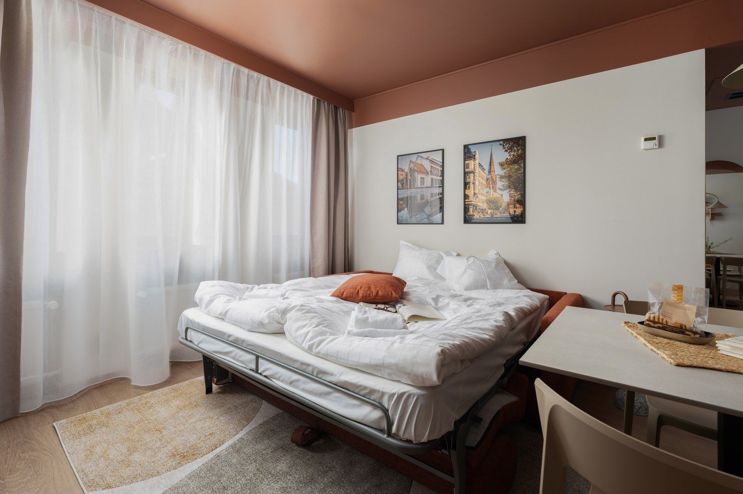 Quarto de hotel com cama, escrivaninha e janela com cortinas.