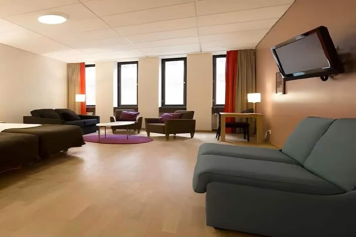 Quarto de hotel com duas camas, um sofá, uma televisão e uma escrivaninha.