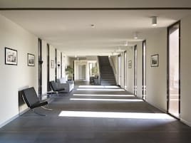 Um corredor moderno com escada, quadros nas paredes e um espaço de estar com um banco e uma cadeira.