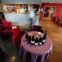 Uma área de bar com balcão, cadeiras vermelhas e uma mesa com garrafas de vinho.