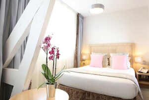 Quarto de hotel com uma cama, mesas de cabeceira, um abajur e uma orquídea em vaso.