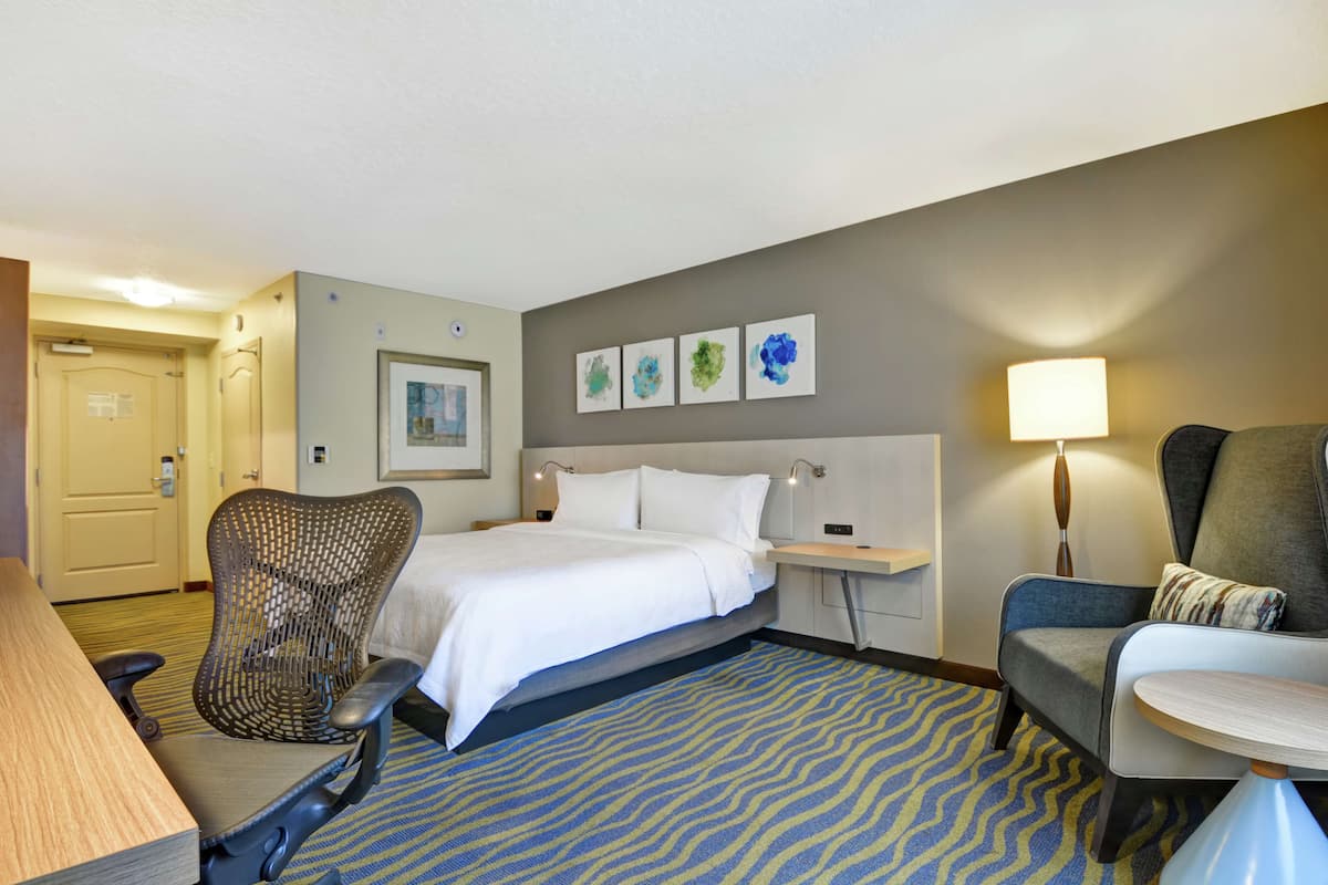 Quarto de hotel com cama, escrivaninha, cadeira, sofá e luminária.