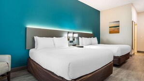Quarto de hotel com duas camas, paredes verde-água, uma cabeceira grande e um quadro na parede.