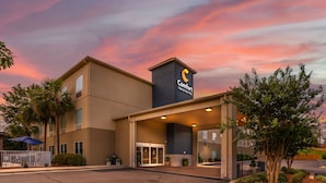 Um hotel Comfort Inn & Suites com entrada visível, palmeiras e céu ao pôr do sol.