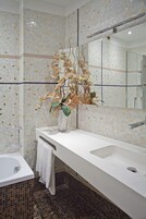 Casa de banho moderna com lavatório branco, cabine de duche em vidro e um arranjo decorativo de orquídeas.