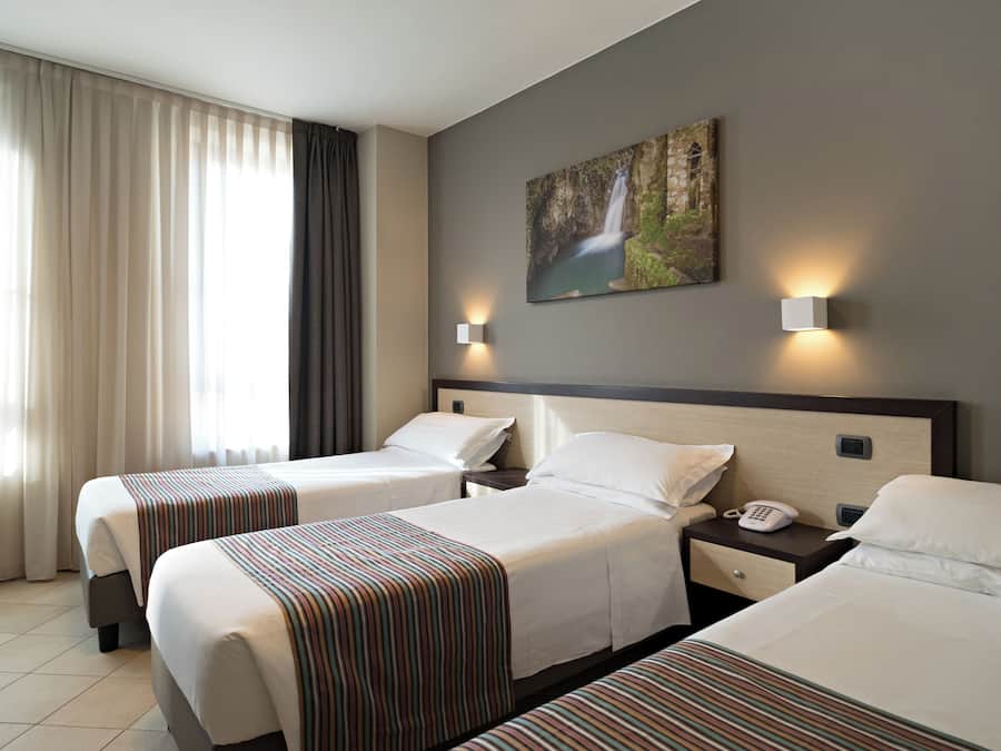 Quarto de hotel com duas camas, um quadro na parede e uma janela com cortinas.