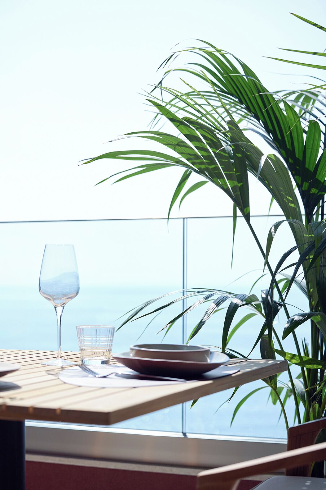 Uma mesa com um copo de água e um prato, em frente a uma varanda com vista para o mar.