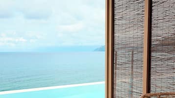Uma varanda com vista para o mar, uma mesa com um copo de água e cadeiras de vime.