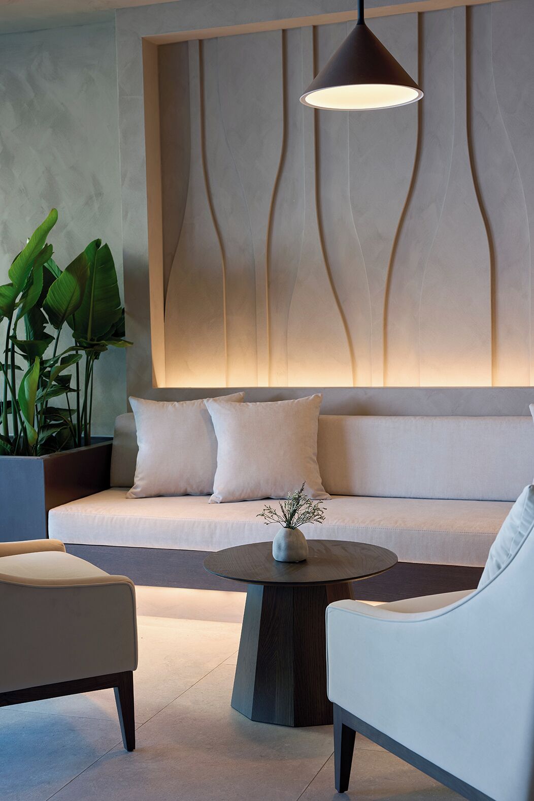 Uma sala de estar moderna com um sofá, duas poltronas, uma mesa de centro e uma luminária pendente.