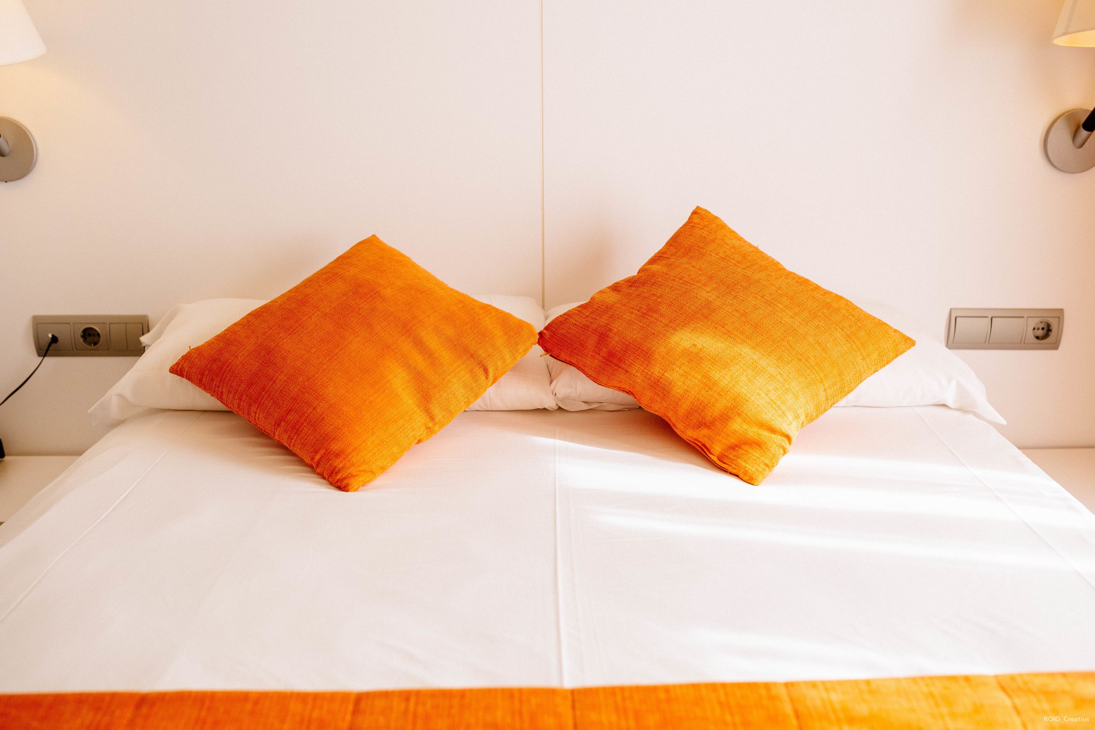 Uma cama com lençóis brancos e duas almofadas laranja.