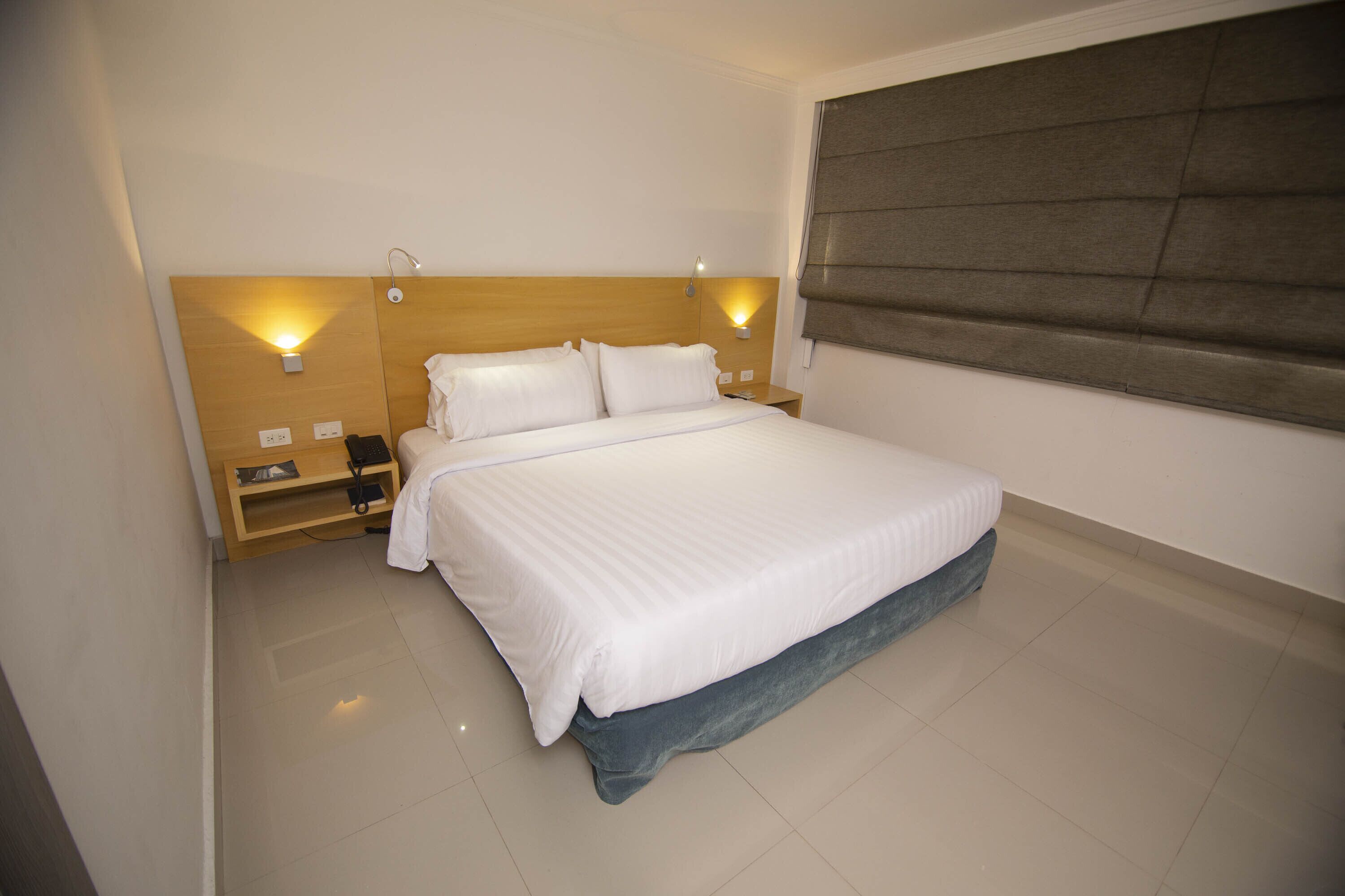 Quarto de hotel com uma cama grande, duas mesas de cabeceira e cabeceira com iluminação integrada.
