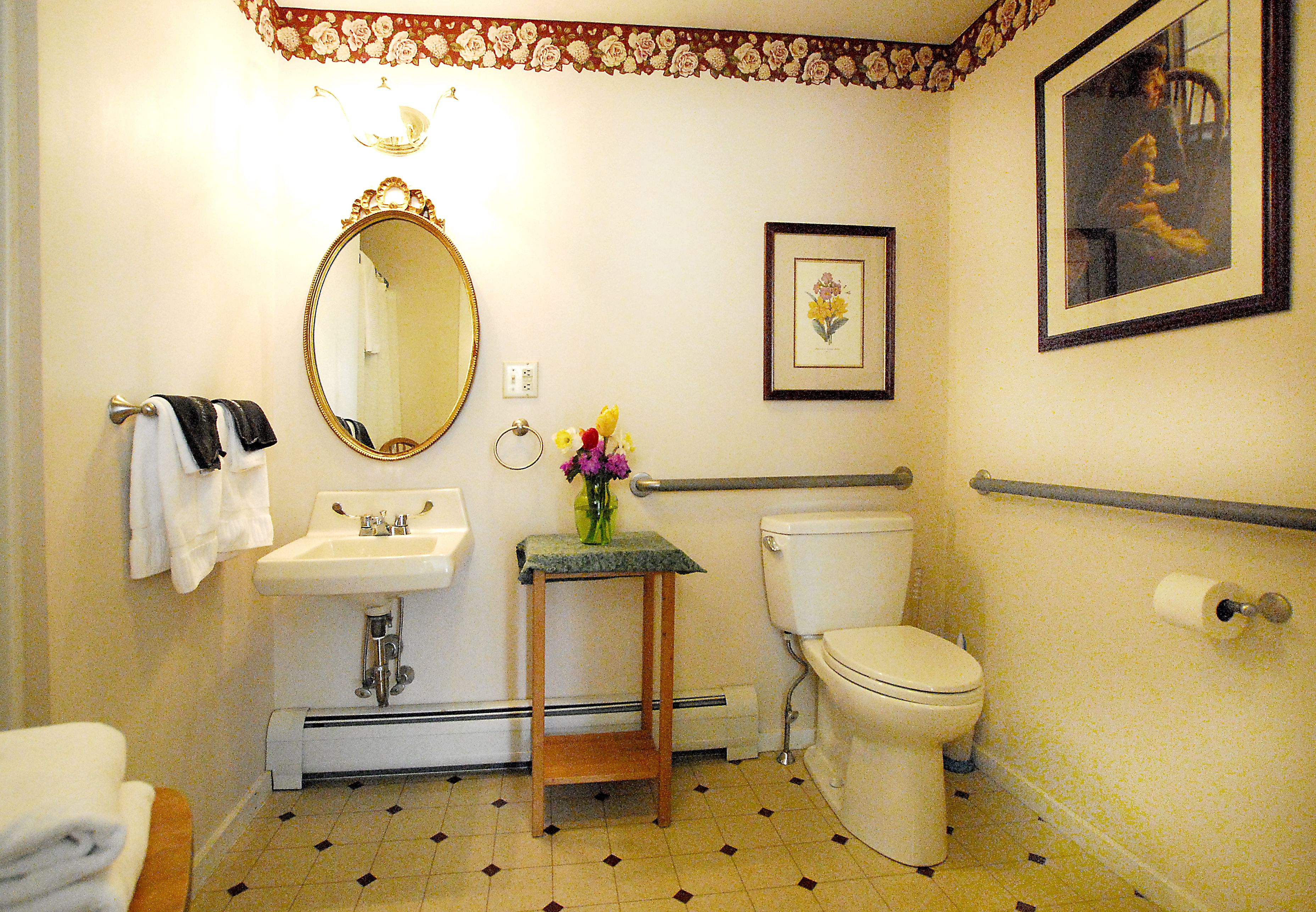 Casa de banho com lavatório, espelho, sanita e uma pequena mesa com um vaso de flores.